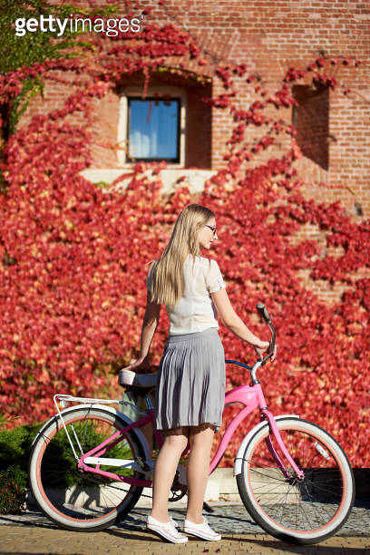 Attractive blond girl at pink lady bicycle on sunny day on wall ...