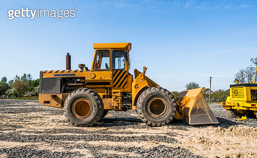 Yellow loader with empty bucket stands on a stone gravel during road ...