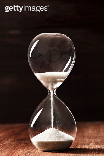 A side view of an hourglass with falling sand, on a dark background ...