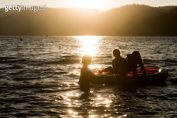 Friends and family playing on an inflatable raft on a beautiful lake at ...