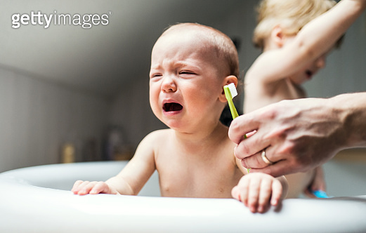 An unhappy baby girl with unrecognizable father crying when brushing ...