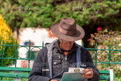Older man sitting on a bench in the Plaza de Armas of Puno checks forms ...