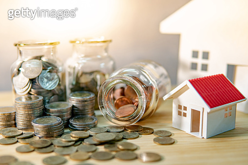 House models with coin in currency glass jars and spilling on wooden ...