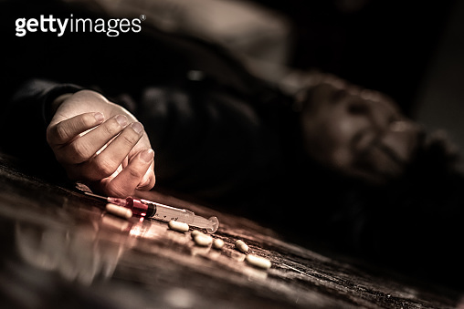 Junkie man lying on the floor near drug injection syringe and pills ...