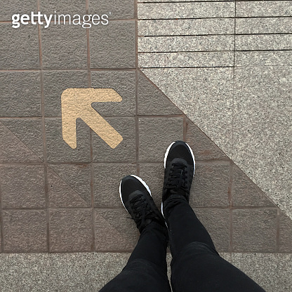 Feet and arrows on road. Yellow sign of arrow direction and standing on ...
