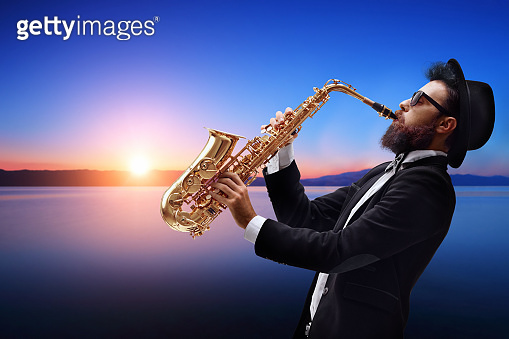 Male jazz musician playing a saxophone with a sunset and water ...