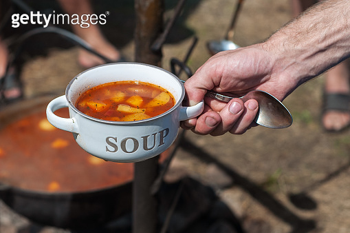 Traditional red soup in a large metal cauldron on a bonfire. Cooking on ...