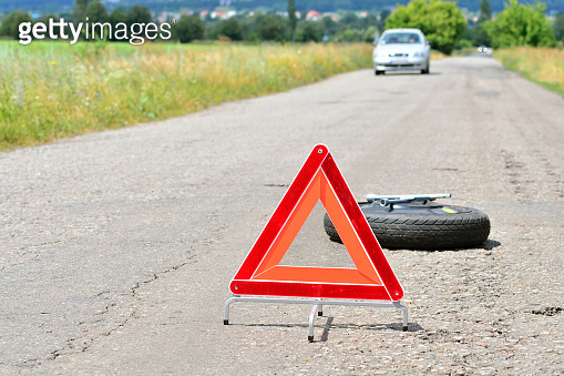 Red emergency triangle stop sign on the road. Spare wheel and wheel ...