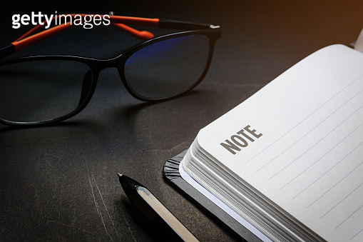 Close up open blank line notebook with black pen and glasses on black ...