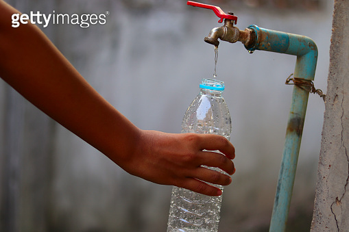Young hand collecting water with a plastic bottle from an old slow ...