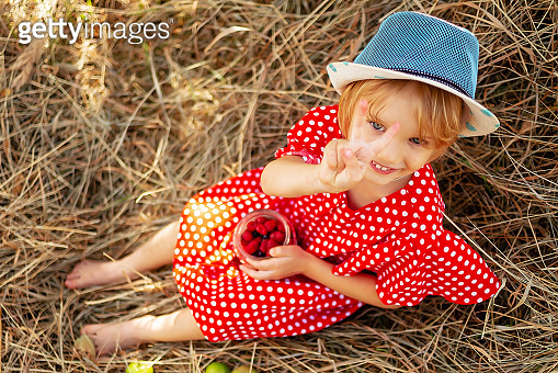 LIttle girl in polka dot red dress and straw hat sitting on a haystack ...