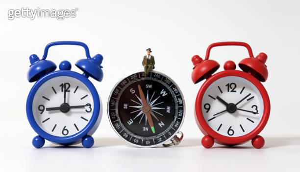 A miniature man sitting on the compass between two alarm clock. 이미지 ...
