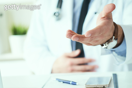 Male doctor making welcome gesture, politely inviting patient to sit ...