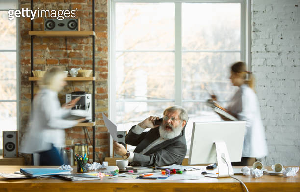 Nervous and tired boss at his workplace busy while people moving near ...