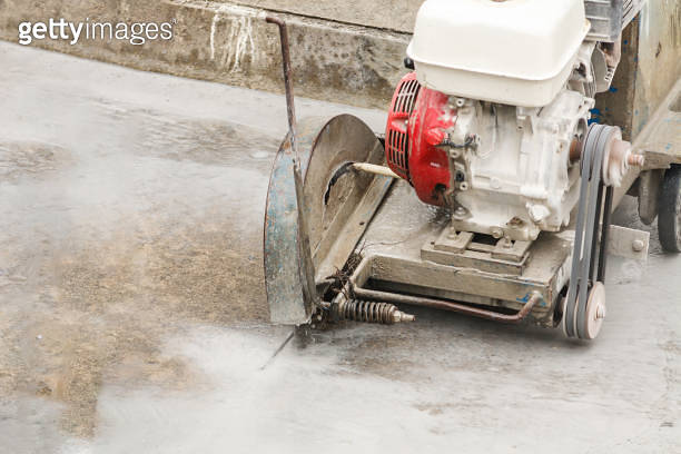 Worker using diamond saw blade machine cutting concrete road at ...