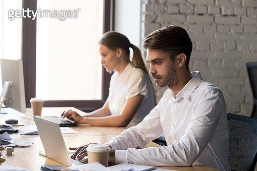 Millennial office worker typing on computer working at shared office ...