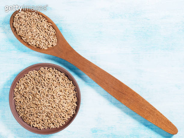 Cumin seeds (Cuminum), Jeera in a clay plate and spoon on a blue wooden ...