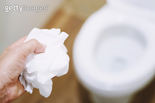 close up hand holding a tissue to be thrown into the toilet bowl. Can ...