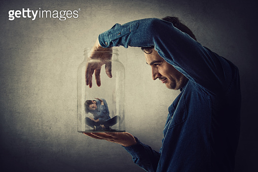 Conceptual scene, scared tiny boy trapped inside a glass jar held in ...