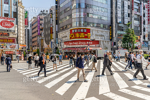 People cross the street at a busy intersection in Shinjuku, in Tokyo ...