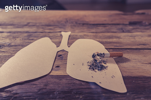 Conceptual image of cigarette burning on paper lungs isolated on rustic ...