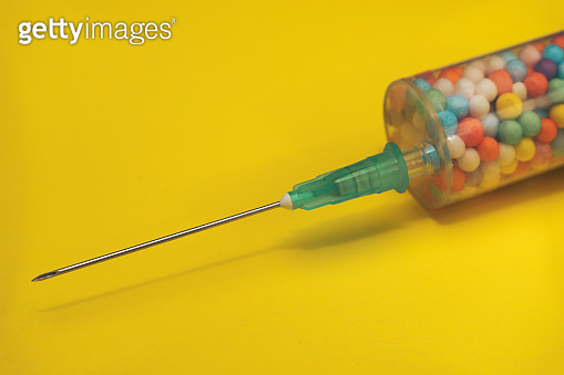 Syringe filled with colorful nano balls on a yellow background ...