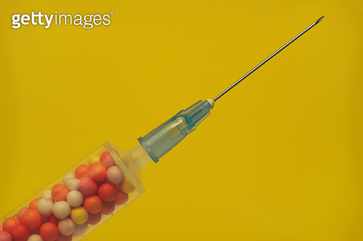 Syringe filled with colorful nano balls on a yellow background ...