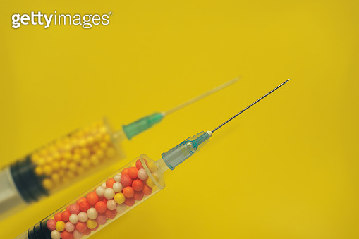 Two syringe filled with colorful nano balls on a yellow background ...