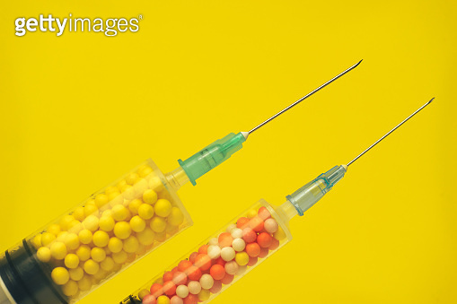 Two syringe filled with colorful nano balls on a yellow background ...