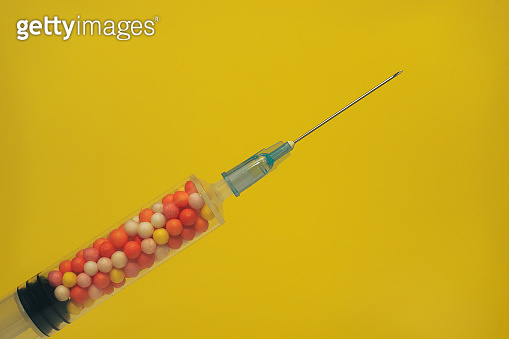 Syringe filled with colorful nano balls on a yellow background ...