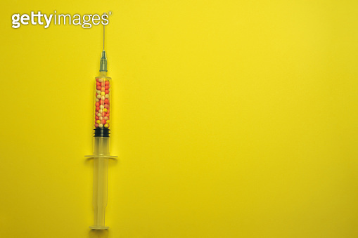 Syringe filled with colorful nano balls on a yellow background ...