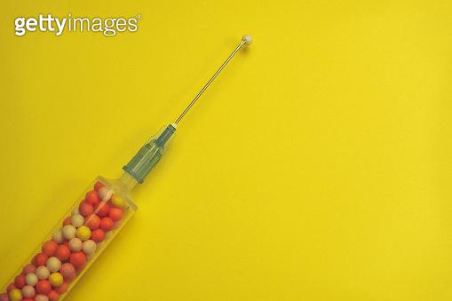 Syringe filled with colorful nano balls on a yellow background ...