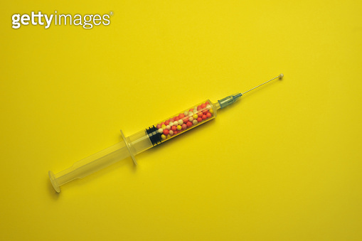 Syringe filled with colorful nano balls on a yellow background ...