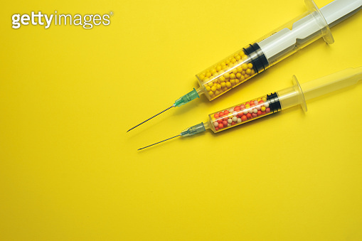 Two syringe filled with colorful nano balls on a yellow background ...