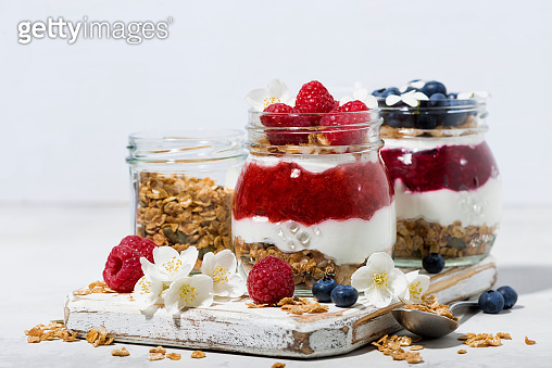sweet desserts with granola, berry and fruit puree in jars on white ...