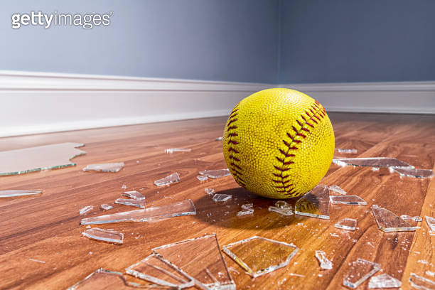 A yellow softball sitting with broken glass from a window on the floor ...