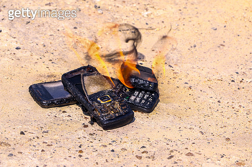 burnt mobile phones on textural concrete background. Concept: Danger of ...