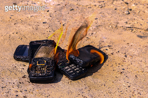 burnt mobile phones on textural concrete background. Concept: Danger of ...