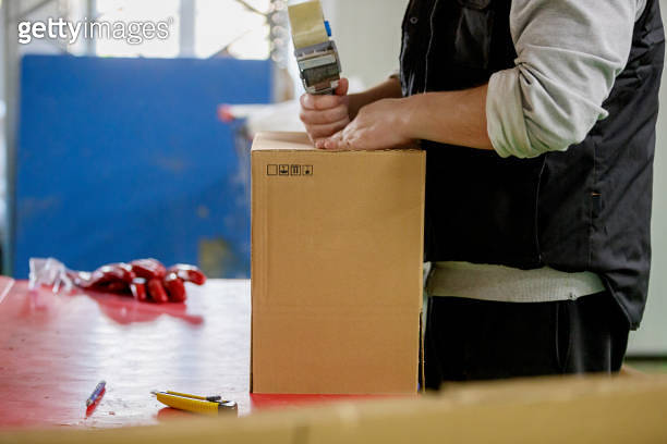 Worker closing cardboard box with tape gun in hand (1166168572) - 게티이미지뱅크