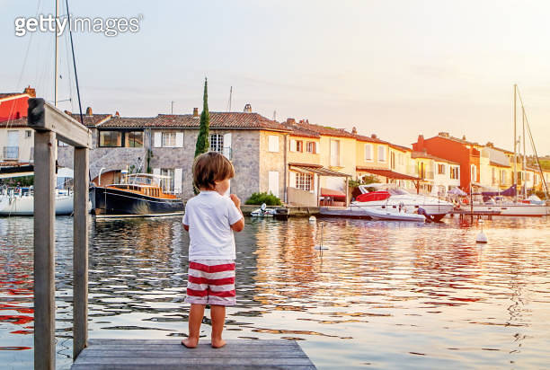 Back view of little boy standing on wooden jetty enjoying sunset view ...