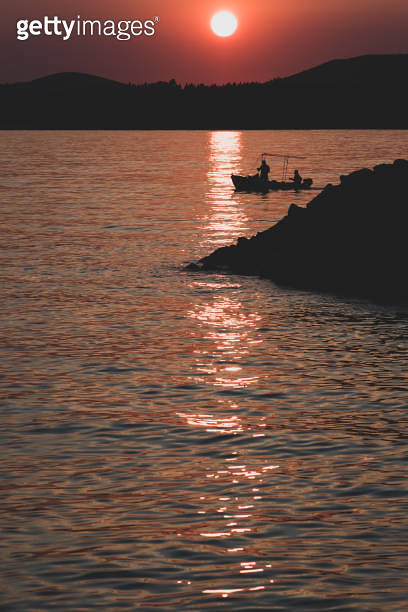 Setting sun, water break of a harbour and silhouette of small fishing ...