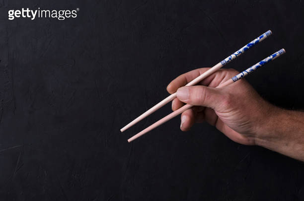 Man using traditional wooden chopsticks, dark background.Blank space ...