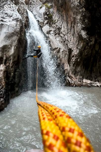 A canyoneer abseiling down a small waterfall in a canyon (1190355931 ...