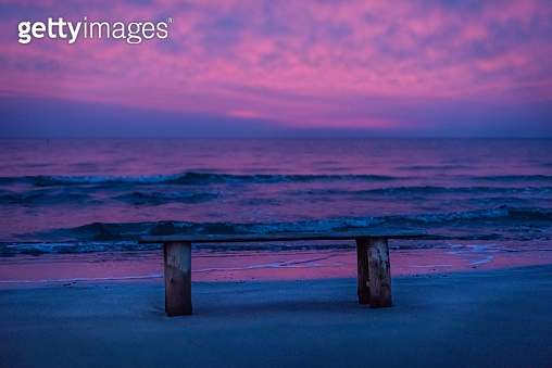 Sunrise on the beach with waves splashing against the shore and wooden ...