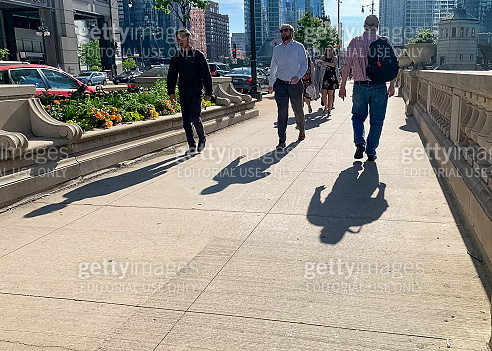 Commuters cast long summer shadows on the sidewalk during rush hour in ...