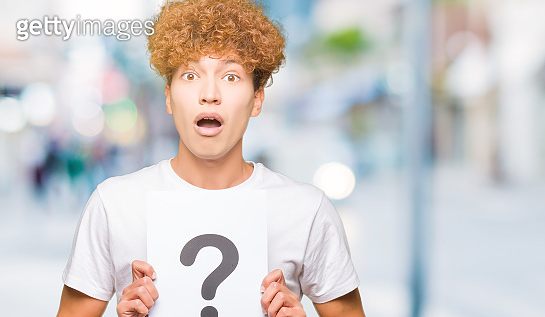 Young handsome man holding paper with question mark scared in shock ...
