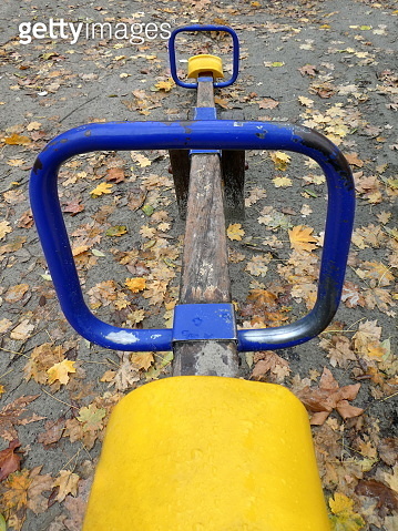 Empty seesaw teeter with yellow seats on playground in autumn, leaves ...
