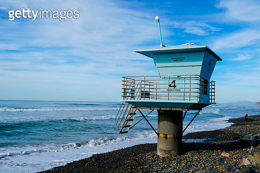 Blue lifeguard tower on a rocky sand beach with clouded blue sky sunny ...