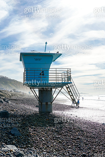 Blue lifeguard tower on a rocky sand beach with clouded blue sky sunny ...