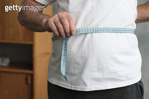 Man measuring his belly with measurement tape standing in the living ...